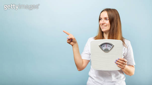 Woman with weighing scale pointing with finger to side on blue ...