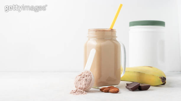 Chocolate whey protein powder in measuring spoon, glass jar of protein ...