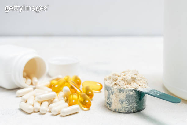 Whey protein powder in measuring spoon, white capsules of amino acids ...