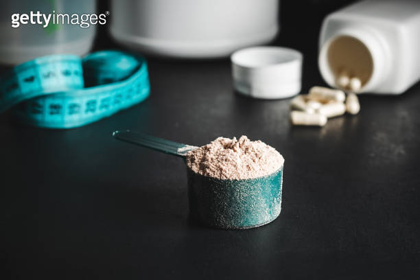 Chocolate whey protein powder in measuring spoon, white capsules of ...