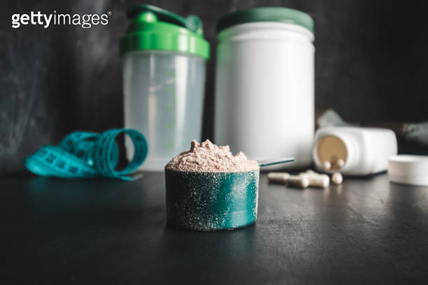 Chocolate whey protein powder in measuring spoon, white capsules of ...