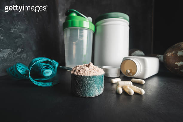 Chocolate whey protein powder in measuring spoon, white capsules of ...