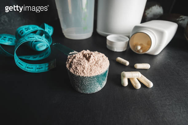 Chocolate whey protein powder in measuring spoon, white capsules of ...