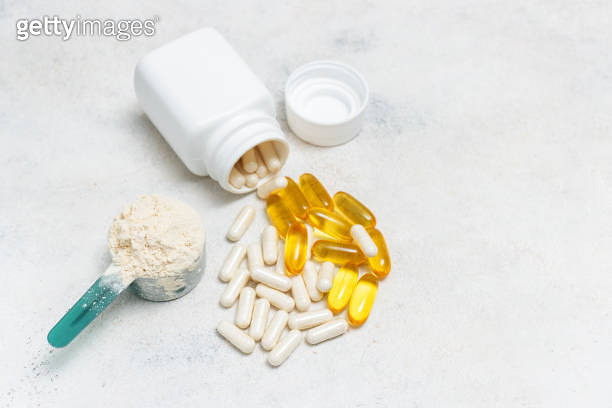 Whey protein powder in measuring spoon, white capsules of amino acids ...