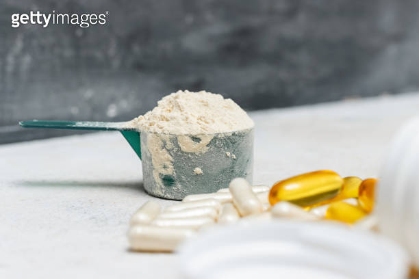 Whey protein powder in measuring spoon, white capsules of amino acids ...