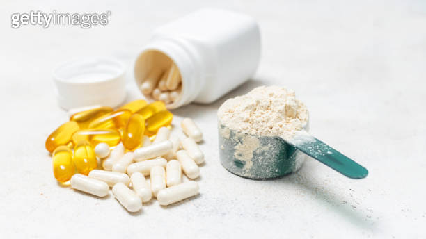 Whey protein powder in measuring spoon, white capsules of amino acids ...