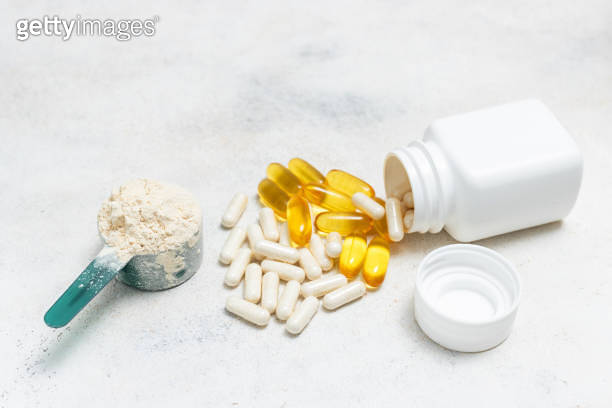 Whey protein powder in measuring spoon, white capsules of amino acids ...