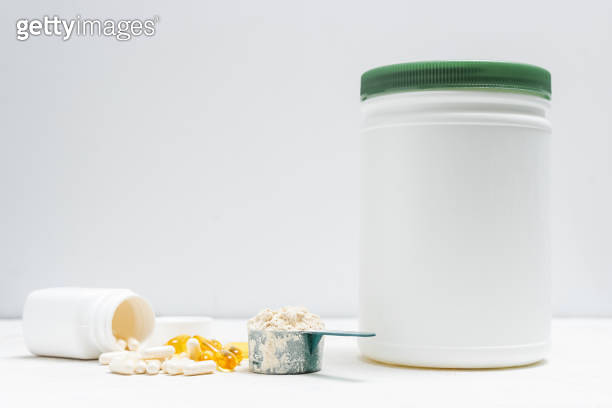 Whey protein powder in measuring spoon, white capsules of amino acids ...