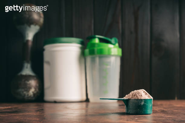 Chocolate whey protein powder in measuring spoon, old rusty dumbbell ...