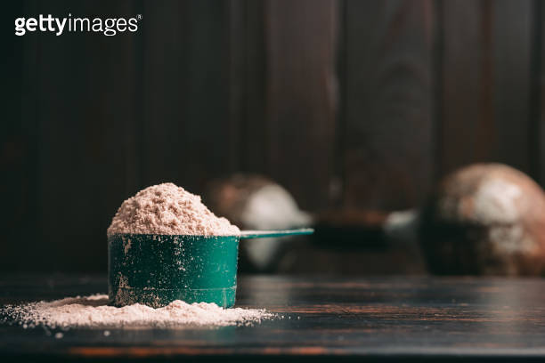 Chocolate whey protein powder in measuring spoon, old rusty dumbbell on ...