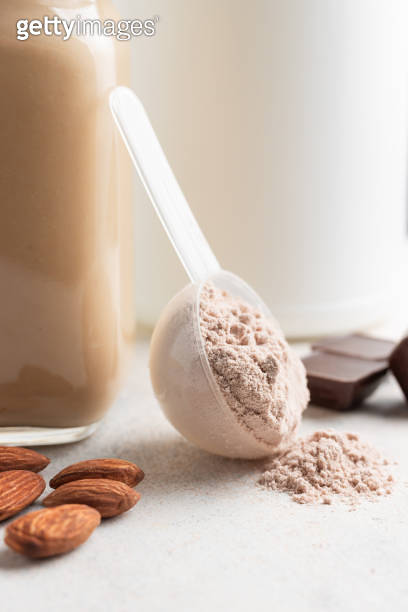 Chocolate whey protein powder in measuring spoon, glass jar of protein ...