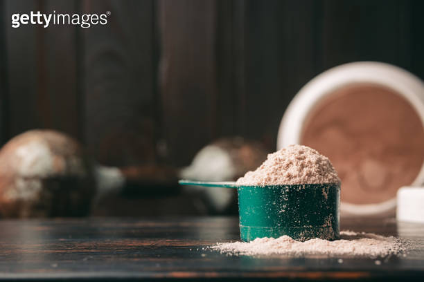Chocolate whey protein powder in measuring spoon, old rusty dumbbell ...