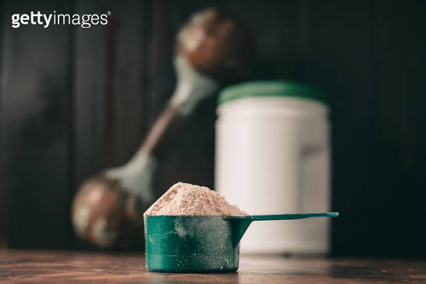 Chocolate whey protein powder in measuring spoon, old rusty dumbbell ...