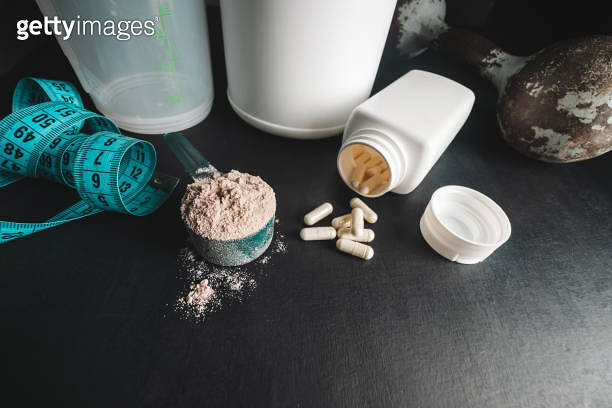 Chocolate whey protein powder in measuring spoon, white capsules of ...