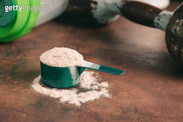 Chocolate whey protein powder in measuring spoon, old rusty dumbbell ...