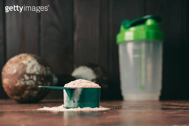 Chocolate whey protein powder in measuring spoon, old rusty dumbbell ...