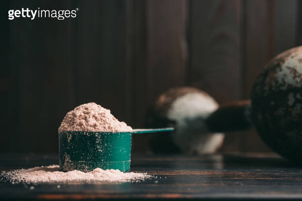 Chocolate whey protein powder in measuring spoon, old rusty dumbbell on ...