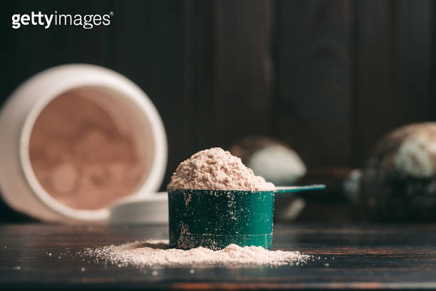 Chocolate whey protein powder in measuring spoon, old rusty dumbbell ...