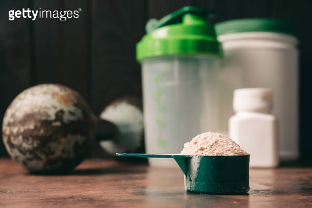 Chocolate whey protein powder in measuring spoon, old rusty dumbbell ...