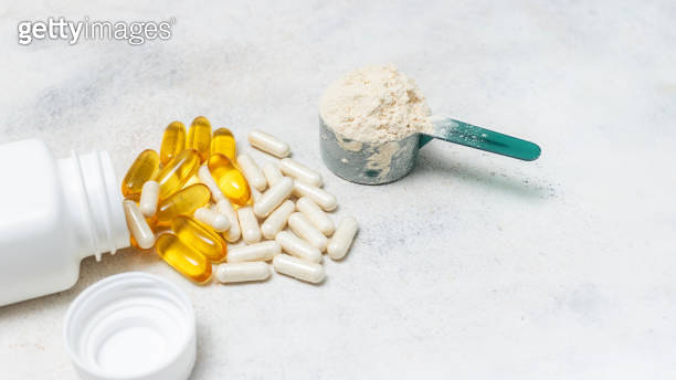Whey protein powder in measuring spoon, white capsules of amino acids ...