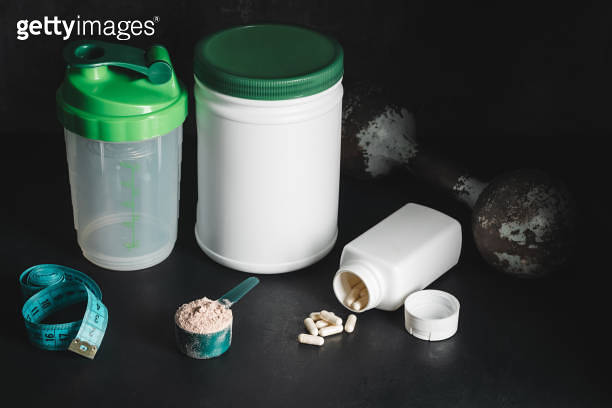 Chocolate whey protein powder in measuring spoon, white capsules of ...