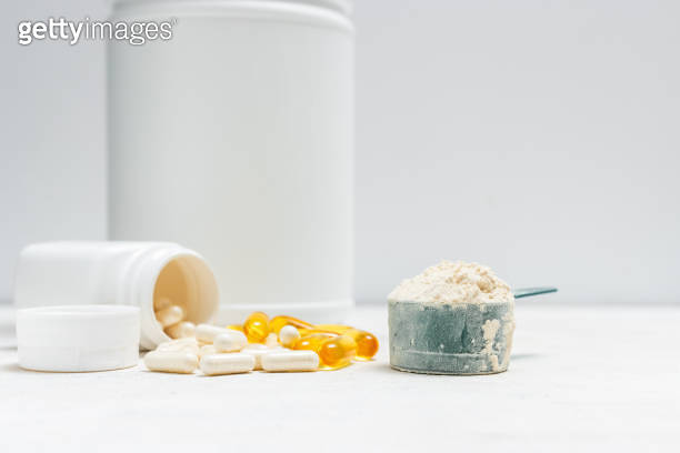 Whey protein powder in measuring spoon, white capsules of amino acids ...