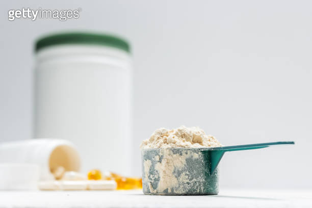 Whey protein powder in measuring spoon, white capsules of amino acids ...