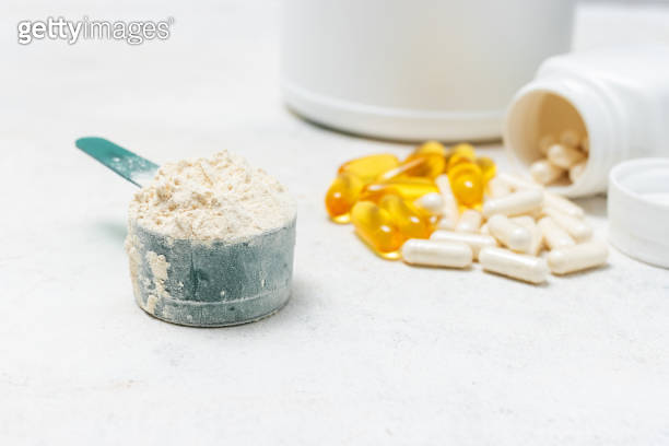 Whey protein powder in measuring spoon, white capsules of amino acids ...