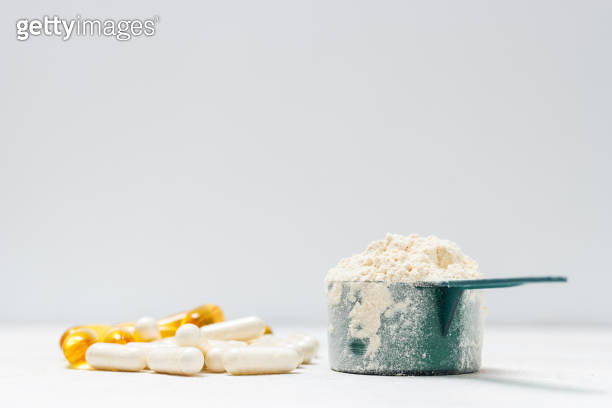 Whey protein powder in measuring spoon, white capsules of amino acids ...