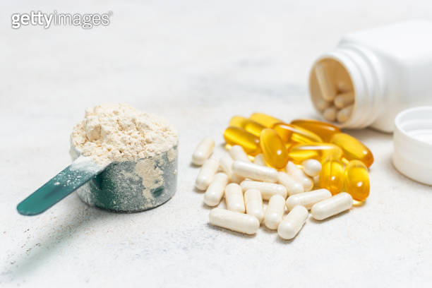 Whey protein powder in measuring spoon, white capsules of amino acids ...