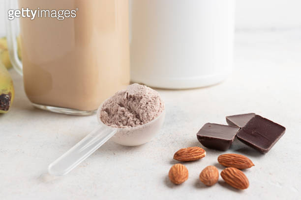 Chocolate whey protein powder in measuring spoon, glass jar of protein ...