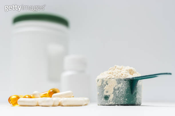 Whey protein powder in measuring spoon, white capsules of amino acids ...