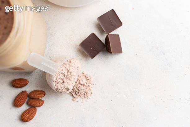 Whey protein powder in measuring spoon, glass jar of protein milkshake ...