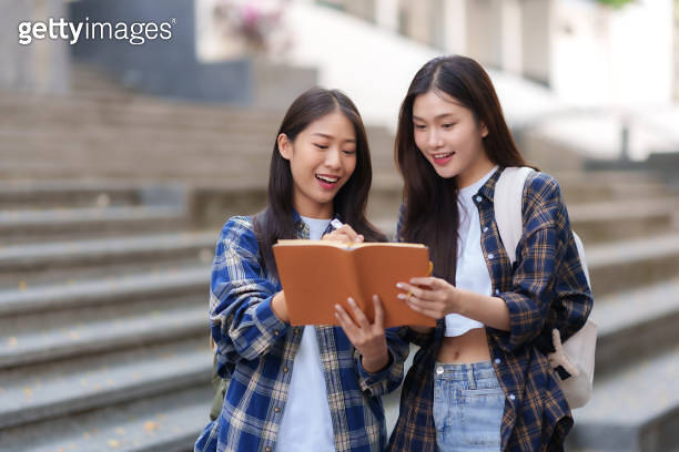 Two Asian students stand reading a book together in university. Young ...