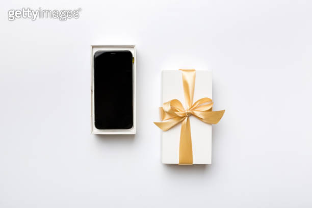 Opened gift box with gold ribbon and smartphone on color background ...