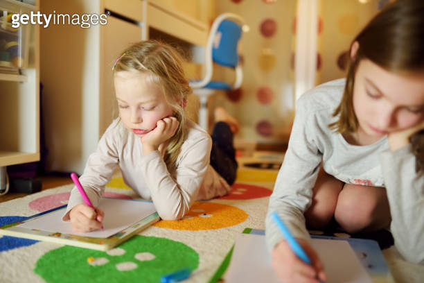 Two cute little sisters writing letters together at home. Older sister ...