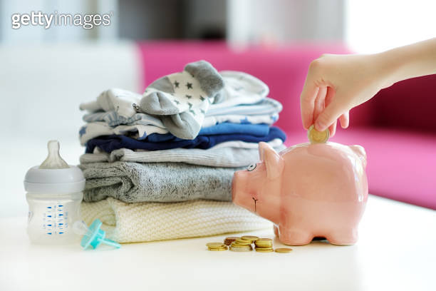 A pile of baby clothes, piggy bank, pacifier and a feeding bottle ...