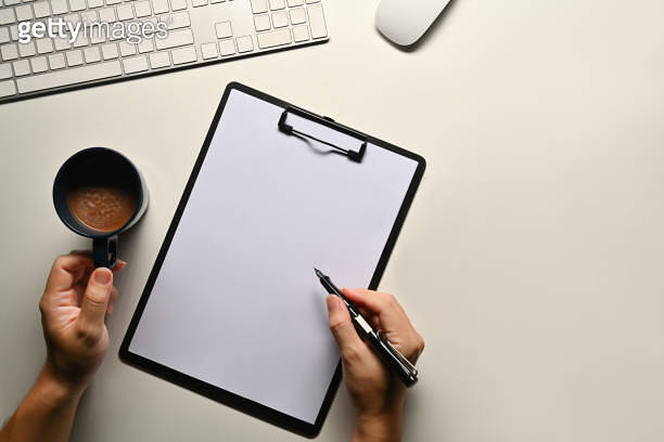 Overhead view of man holding coffee cup and writing on blank paper ...