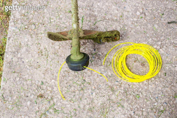 A lawn mower with fishing line after cutting the grass and a roll of ...