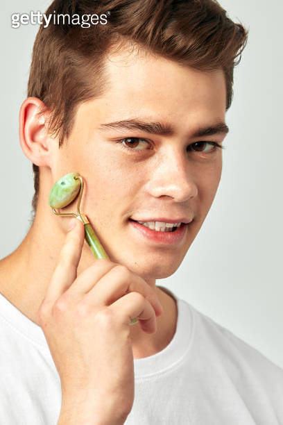 Young handsome smiling brown haired guy using jade de-puffing face ...
