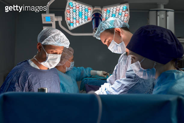 Portrait of surgeons leaned over patient during complex surgical ...