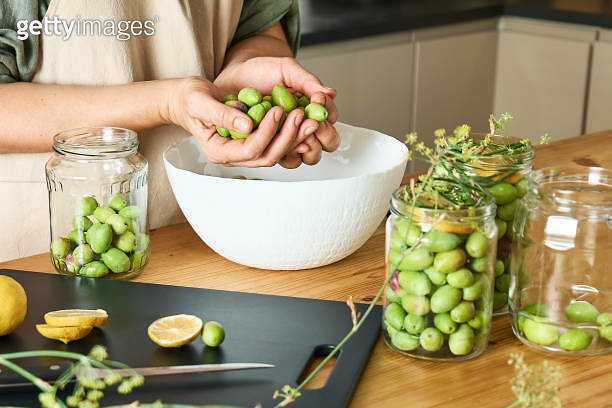 Woman preparing fermented olives in glass jar with slices of lemon ...
