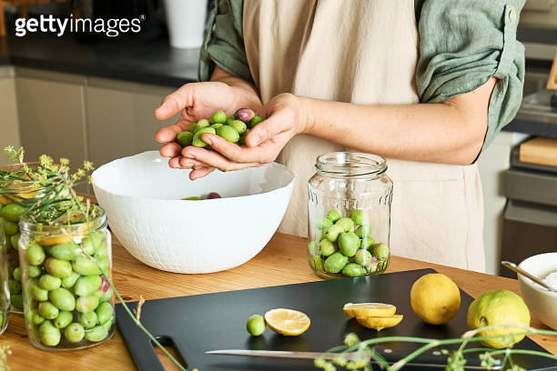 Woman preparing fermented olives in glass jar with slices of lemon ...