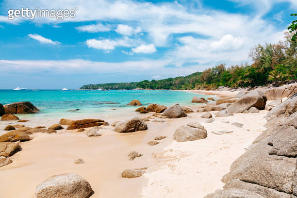 Tropical beach with clear blue water and large rocks on the shore in ...