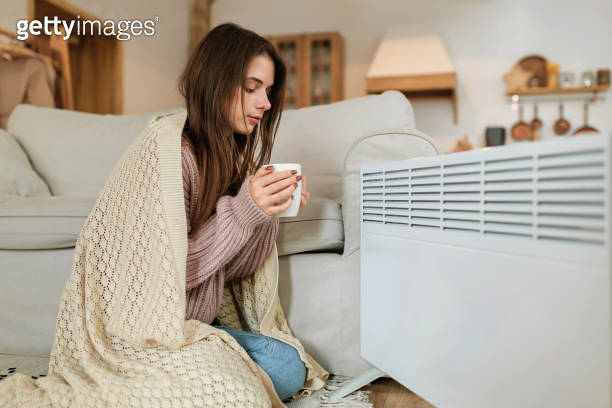Cold home, freezing. Using heater at home in winter. Woman warming her ...