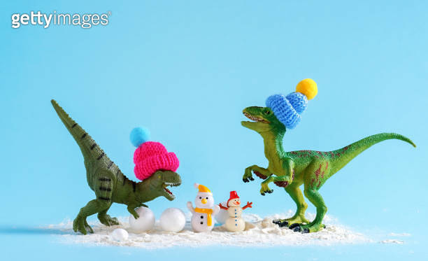 Two cute green dinosaurs in knitted hats build snowman. Cute funny ...