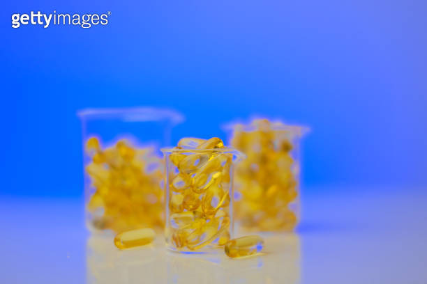Fish oil capsules in transparent flasks on a blue background.Natural ...