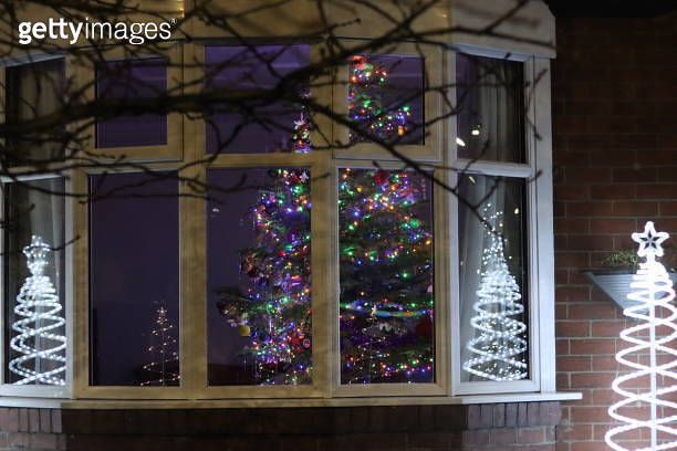 Christmas tree at night through a house window, covered in lights and ...