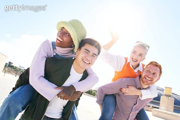 Piggyback multiracial couples smiling together outdoors on a sunny ...