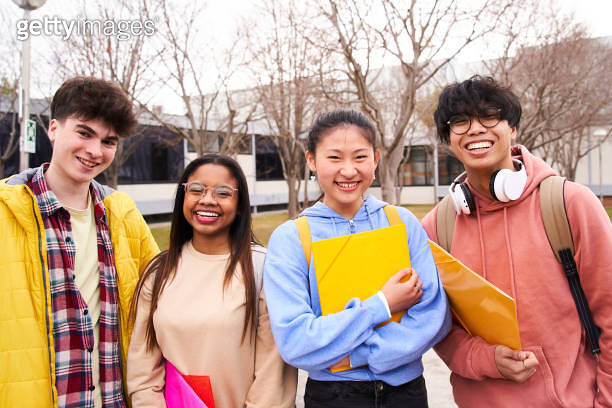 Portrait of a group of four students standing up and looking at camera ...